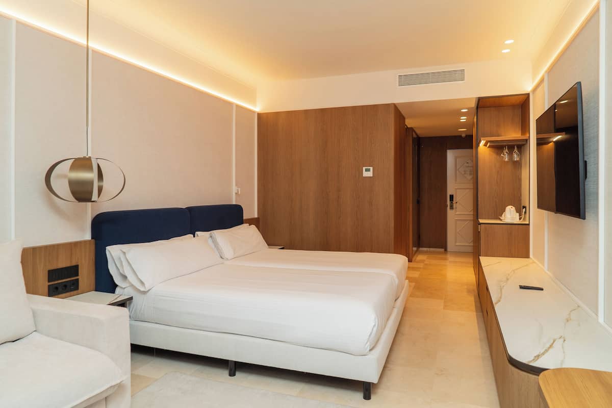 Quarto de hotel moderno com uma cama grande, televisão e guarda-roupa de madeira.