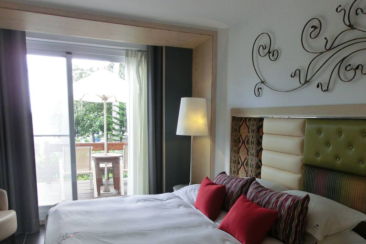 Quarto de hotel com cama, cabeceira, decoração na parede, janela com cortinas e vista para o exterior.