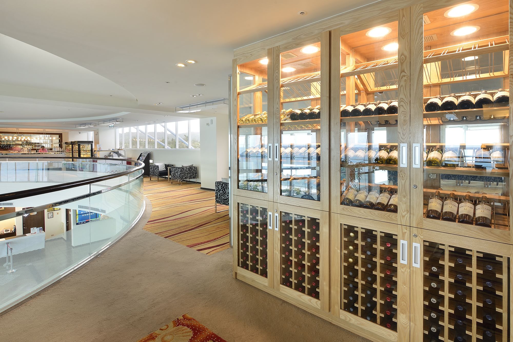 Um saguão de hotel com adega de vinhos, guarda-corpo de vidro e área de estar.