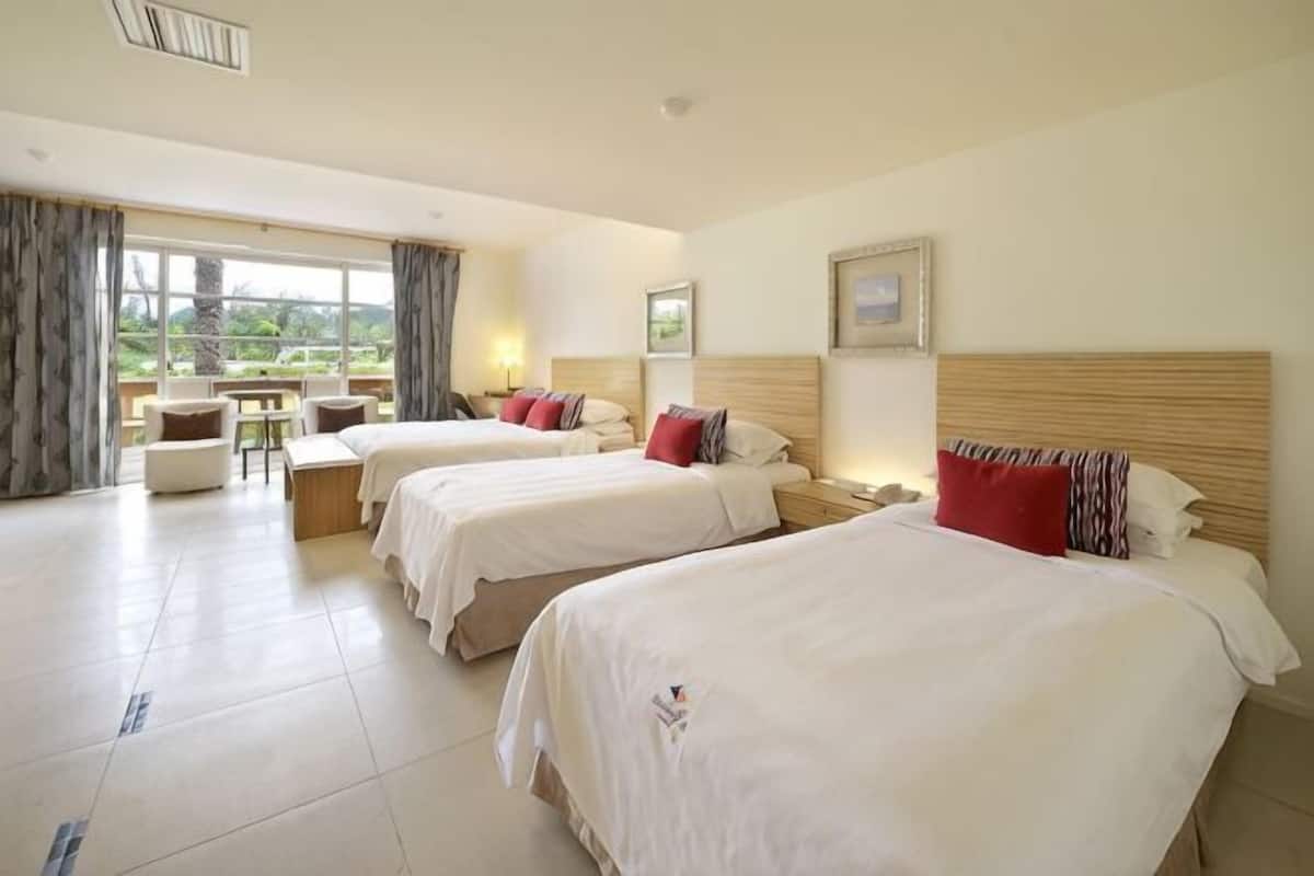 Quarto de hotel com três camas, uma escrivaninha e vista para o exterior.