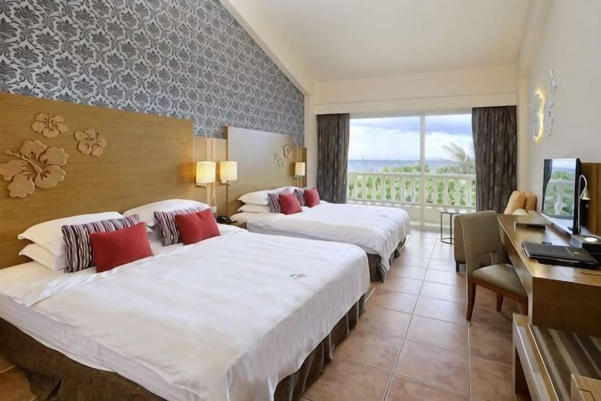 Quarto de hotel com duas camas, uma escrivaninha, uma cadeira e varanda com vista.