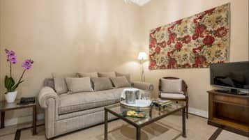 Uma sala de estar com sofá, mesa de centro, rack para TV e um quadro floral na parede.