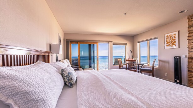 Quarto de hotel com uma cama grande, área de refeições com vista para o oceano e uma parede de destaque em pedra.