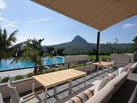 Uma área na beira da piscina com vista para uma montanha, mobiliário externo e um alpendre coberto.