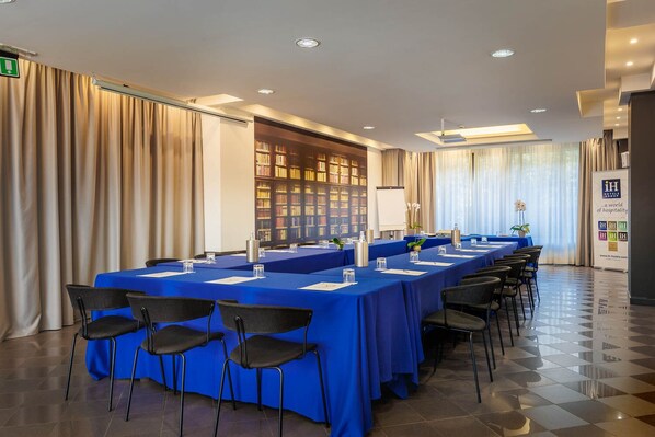 Uma sala de conferências com uma mesa comprida, cadeiras e uma estante de livros ao fundo.