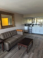 Uma sala de estar com sofá, mesa de centro e área de cozinha com armários e eletrodomésticos.