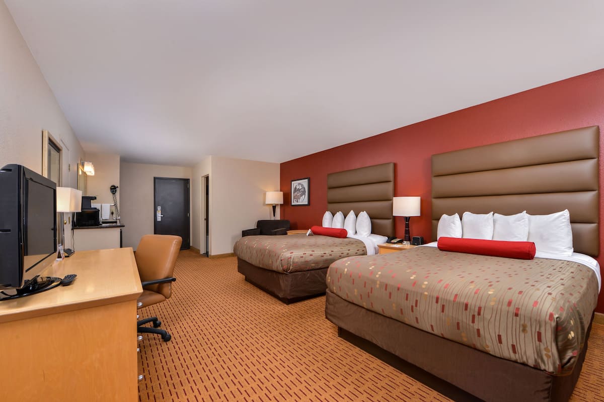 Quarto de hotel com duas camas, uma escrivaninha, uma cadeira e uma televisão.