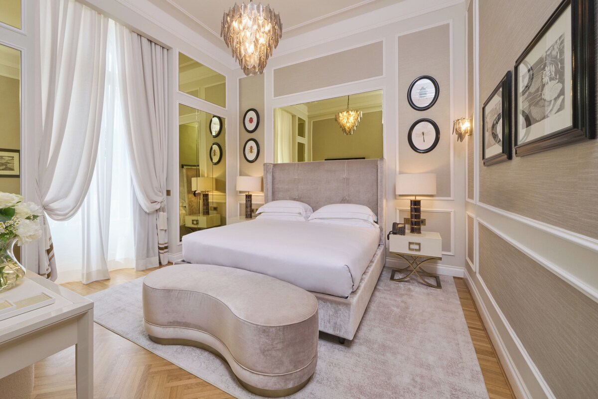 Quarto moderno com uma cama grande, toucador e um candeeiro de cristal.