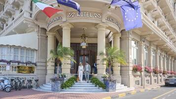 Uma imponente entrada de hotel com colunas, portas duplas e uma placa com a inscrição "HOTEL PRINCIPATE".