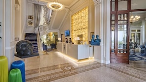 Um hall imponente com escadaria, balcão de recepção e um lustre grande.