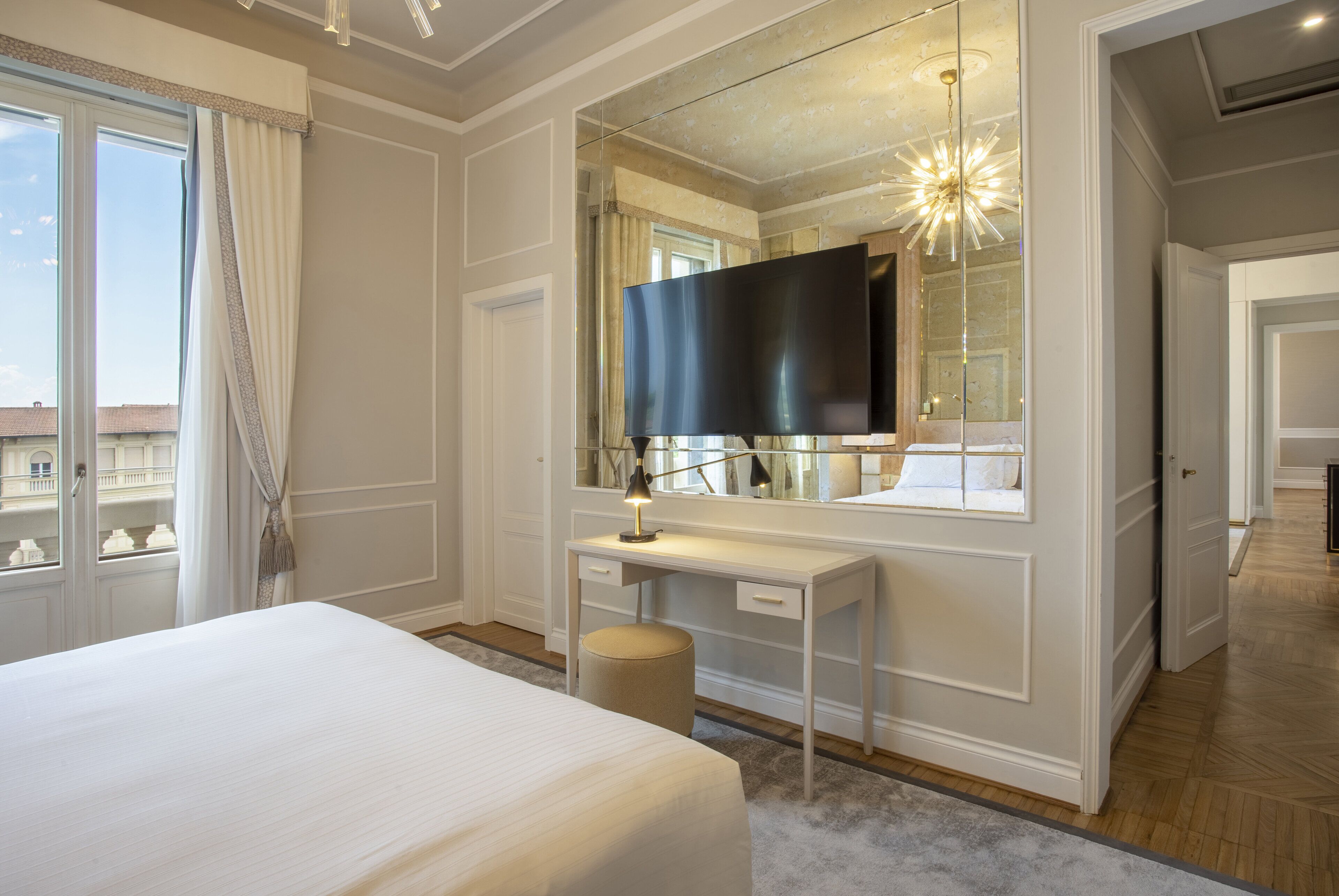 Quarto de hotel com uma cama grande, uma escrivaninha com televisão, um espelho e vista para o exterior.