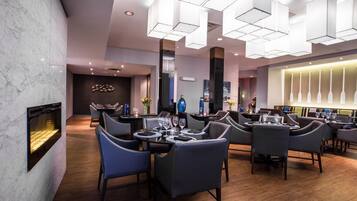 Um restaurante moderno com paredes de mármore, lareira e luminárias contemporâneas.