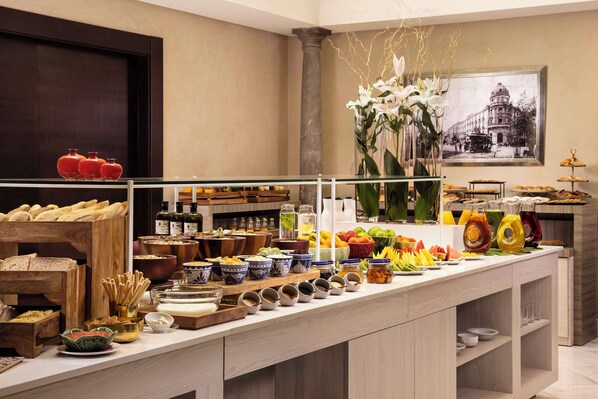 Buffet com diversas opções de comida, incluindo frutas, legumes e pão.