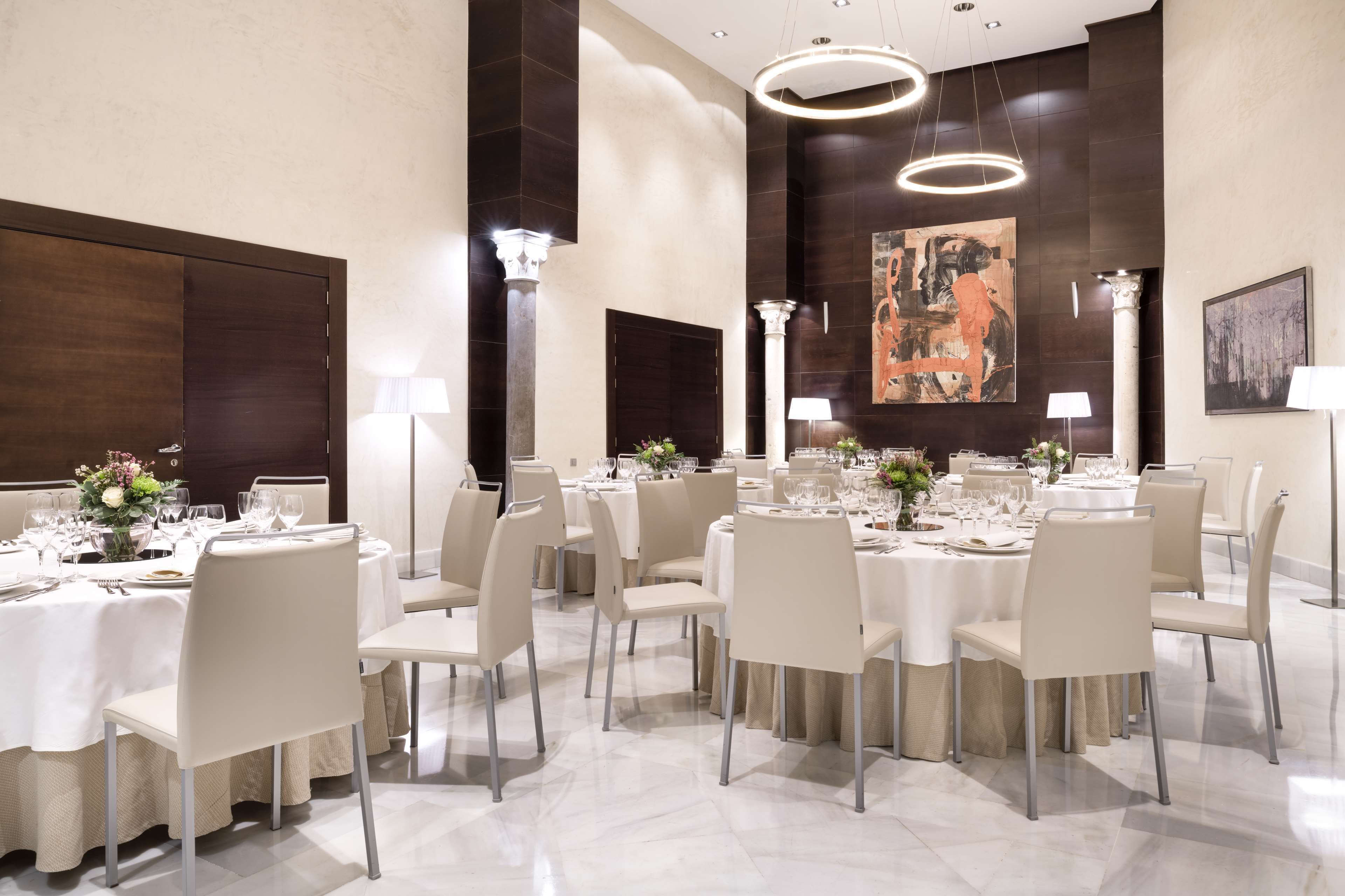 Uma sala de jantar espaçosa com várias mesas redondas dispostas para um evento formal, com toalhas de mesa brancas e cadeiras.
