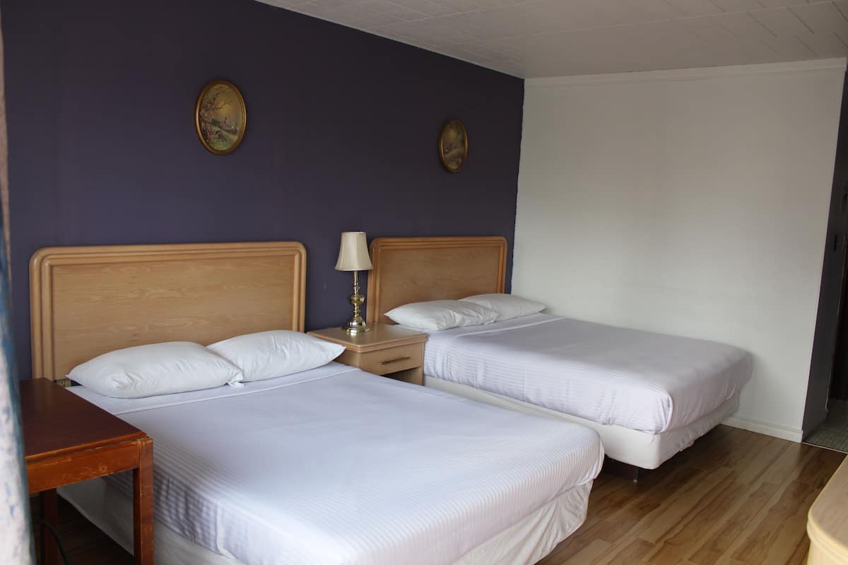 Quarto com duas camas de solteiro, cabeceiras de madeira, uma mesa de cabeceira com abajur e uma pequena mesa.