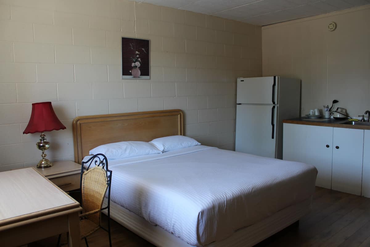 Quarto com cama, escrivaninha, cadeira, luminária vermelha, geladeira e pequena cozinha.