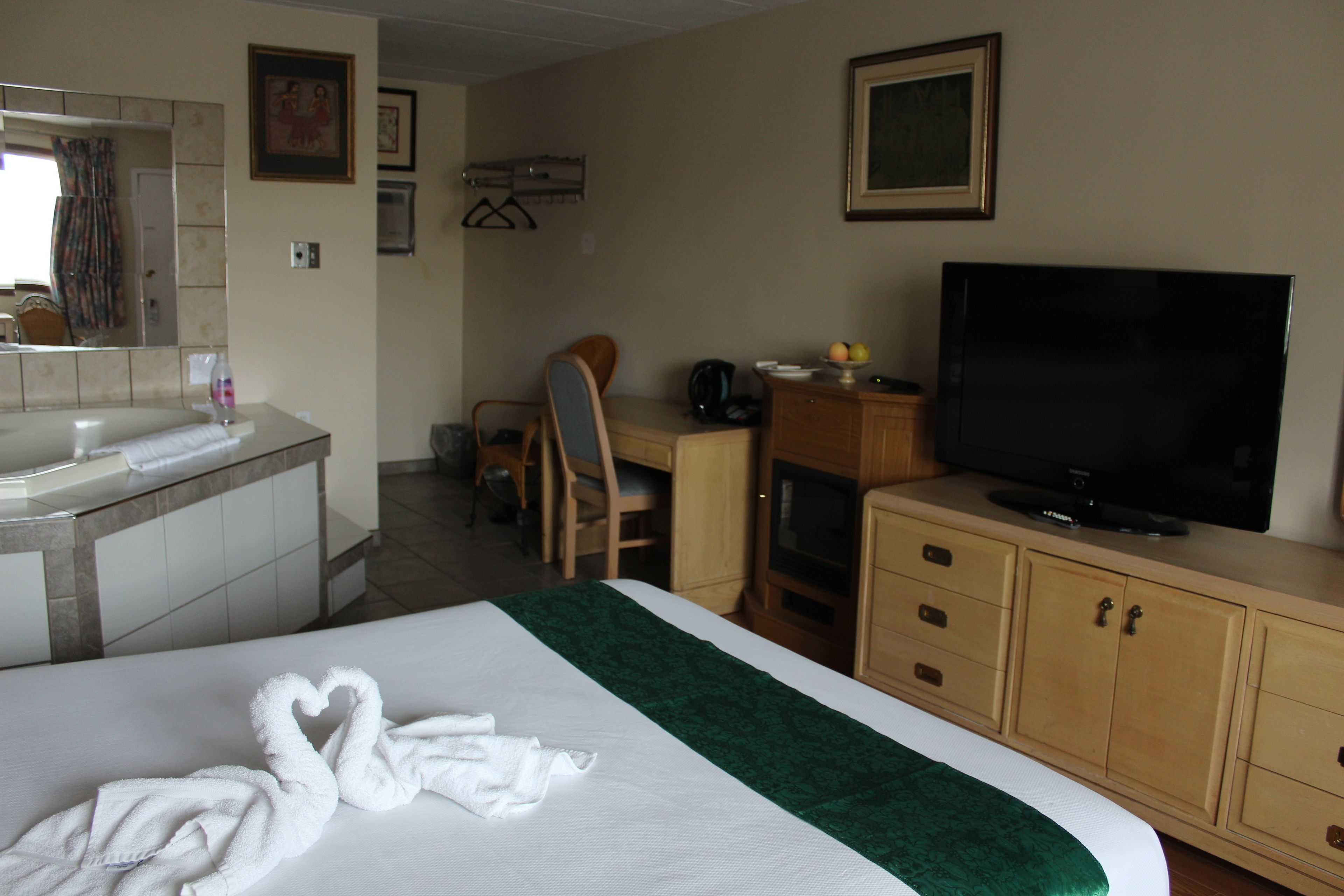Quarto de hotel com cama, escrivaninha, televisão e banheiro com espelho e pia.
