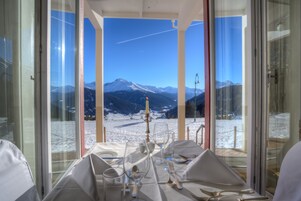 Mesa de jantar posta para dois, com vista para a montanha através de grandes janelas.
