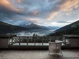 Varanda com cadeira de vime com vista para uma paisagem montanhosa com vale e névoa.