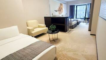 Quarto de hotel com cama, sofá, televisão, uma pequena mesa com uma planta e vista para a cidade pela janela.