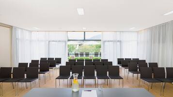 Sala de conferência com fileiras de cadeiras, uma mesa comprida e vista para o verde lá fora.