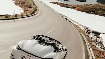 Um carro esportivo branco dirigindo em uma estrada sinuosa com manchas de neve nas laterais.