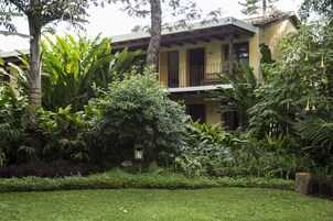 Um edifício com varanda, rodeado por vegetação exuberante e um gramado bem cuidado.