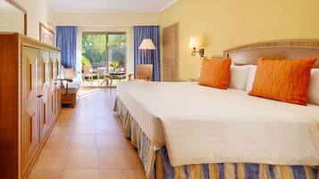 Quarto de hotel com uma cama grande, um guarda-roupa de madeira, uma mesa com cadeira e uma varanda com mesa e cadeiras.