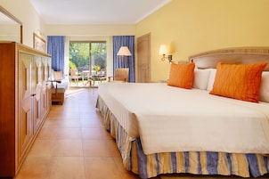 Quarto de hotel com uma cama grande, um guarda-roupa de madeira, uma mesa com cadeira e uma varanda com mesa e cadeiras.