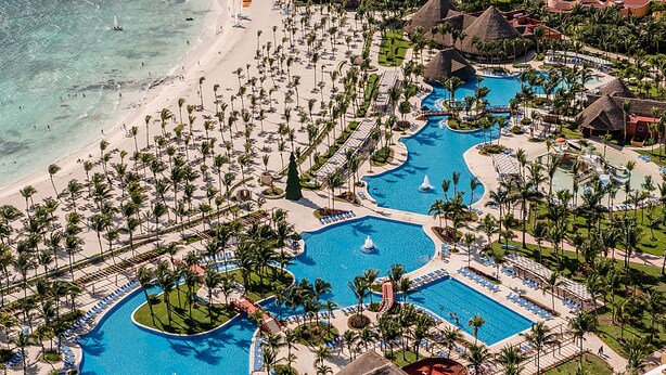 Resort com várias piscinas, palmeiras e acesso à praia.