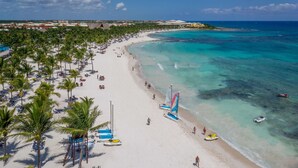 Uma praia com palmeiras, areal e barcos.