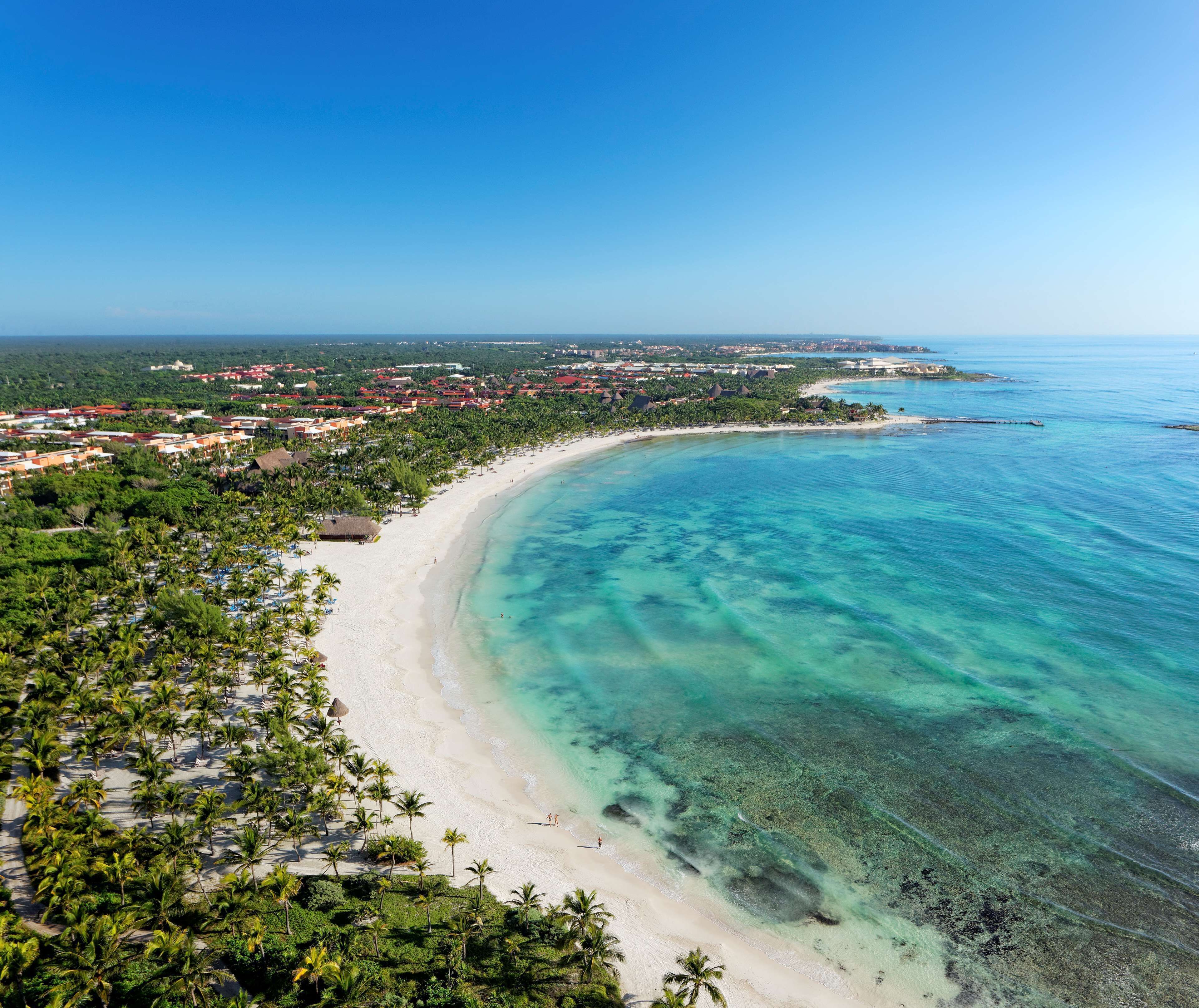 Um resort à beira-mar com uma praia arenosa, águas turquesa cristalinas e vegetação exuberante.