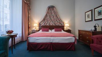 Quarto de hotel com uma cama grande, mesa de cabeceira com abajur, cômoda e uma cadeira.