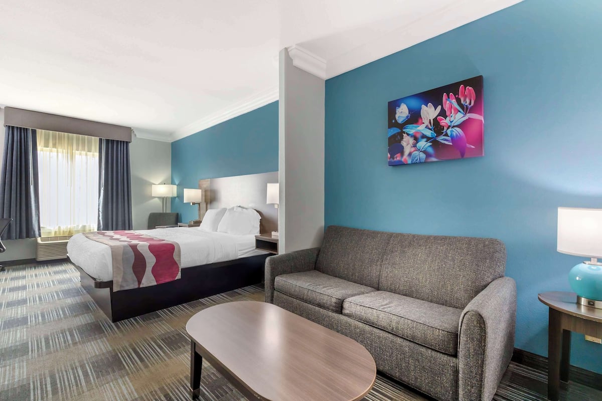 Quarto de hotel com cama, sofá, mesa de centro e um quadro na parede.