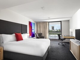 Quarto de hotel com uma cama grande, uma mesa, uma cadeira e vista para a cidade.