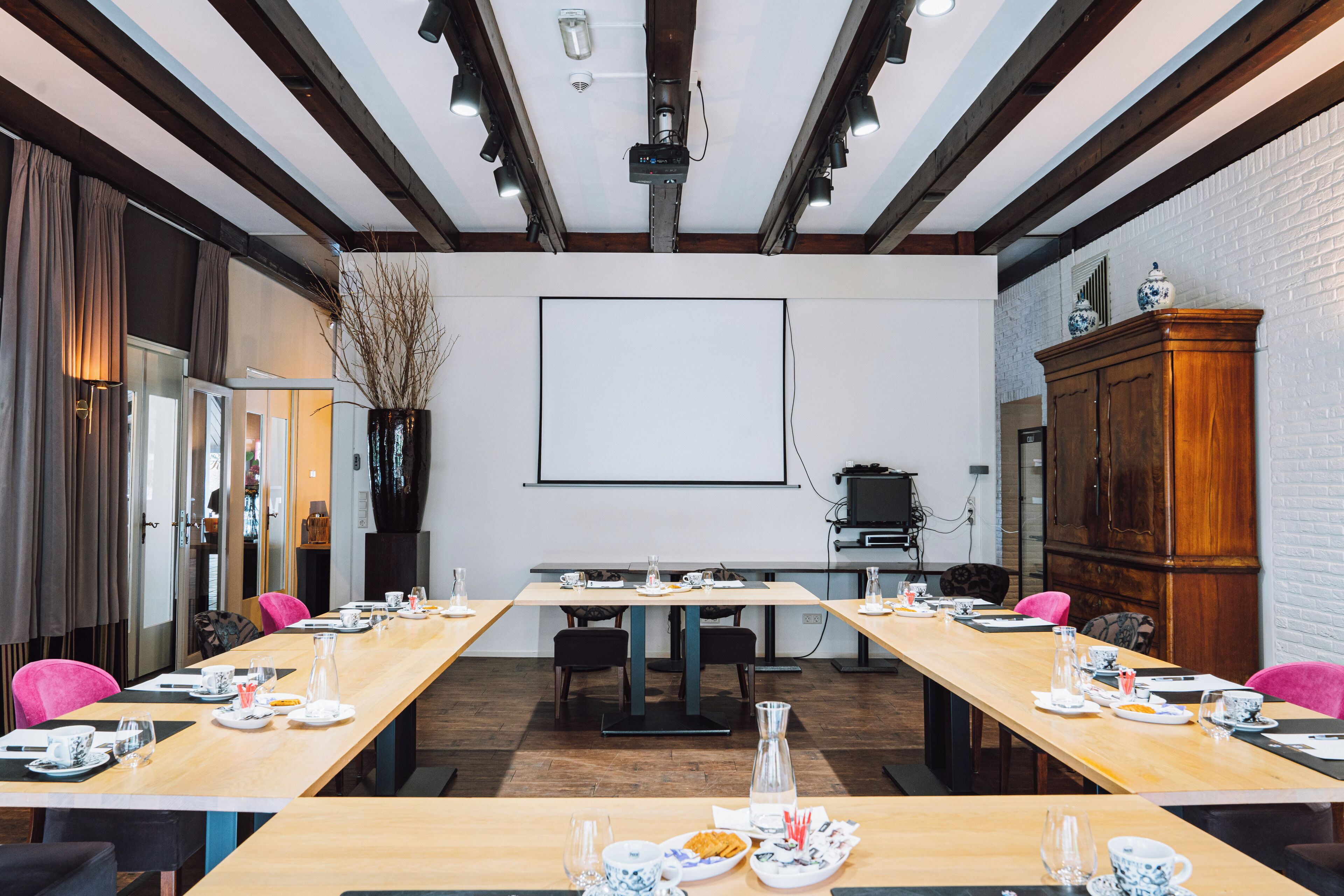 Uma sala de conferências com uma mesa comprida, cadeiras e uma tela de projeção.
