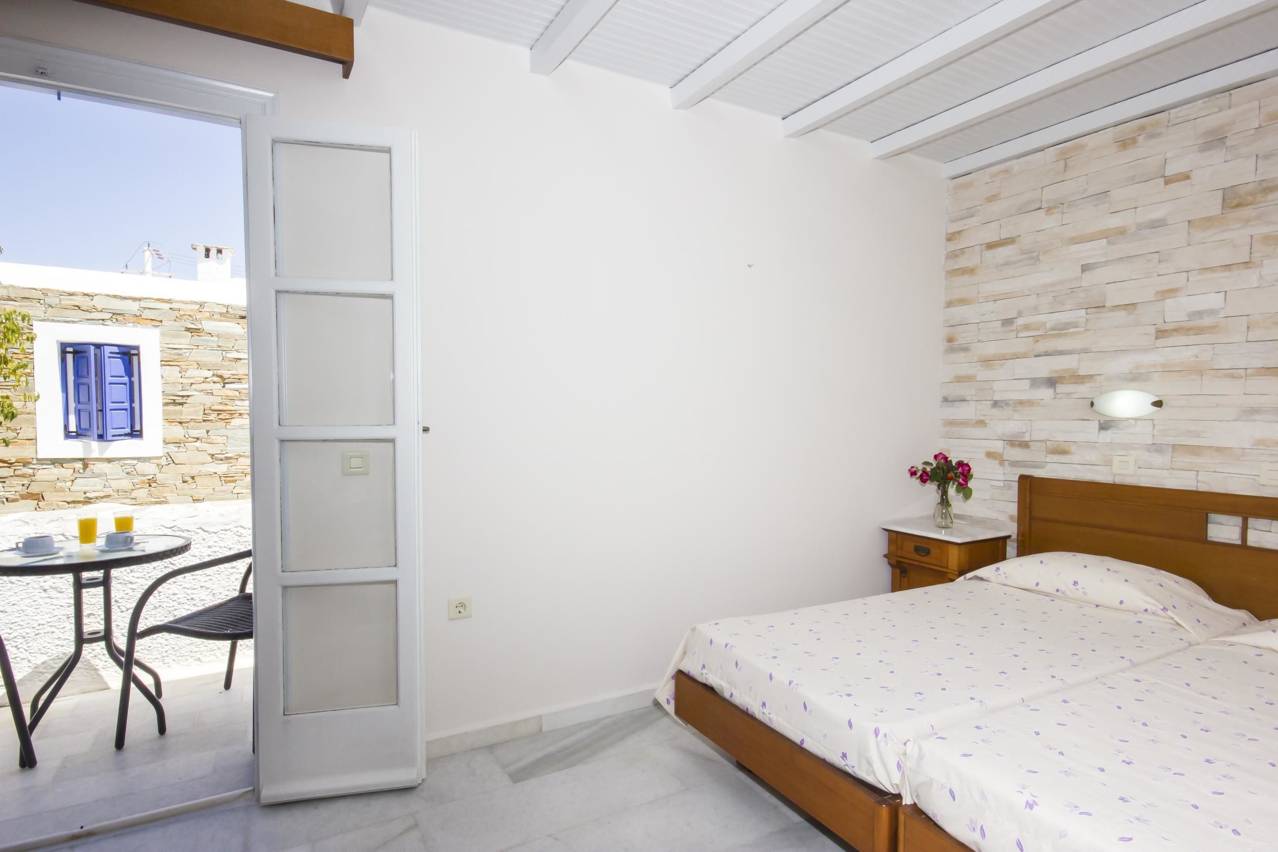 Quarto com cama, mesa de cabeceira com abajur, pequena mesa com cadeira e vista para o exterior.