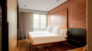 Quarto de hotel moderno com parede de tijolos, uma janela grande com cortinas finas, uma cama com roupa de cama branca e uma poltrona de couro.