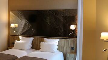 Quarto de hotel com duas camas, um espelho grande e uma cabeceira de madeira.