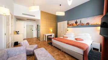 Quarto de hotel com uma cama, duas cadeiras, uma escrivaninha e um quadro na parede.