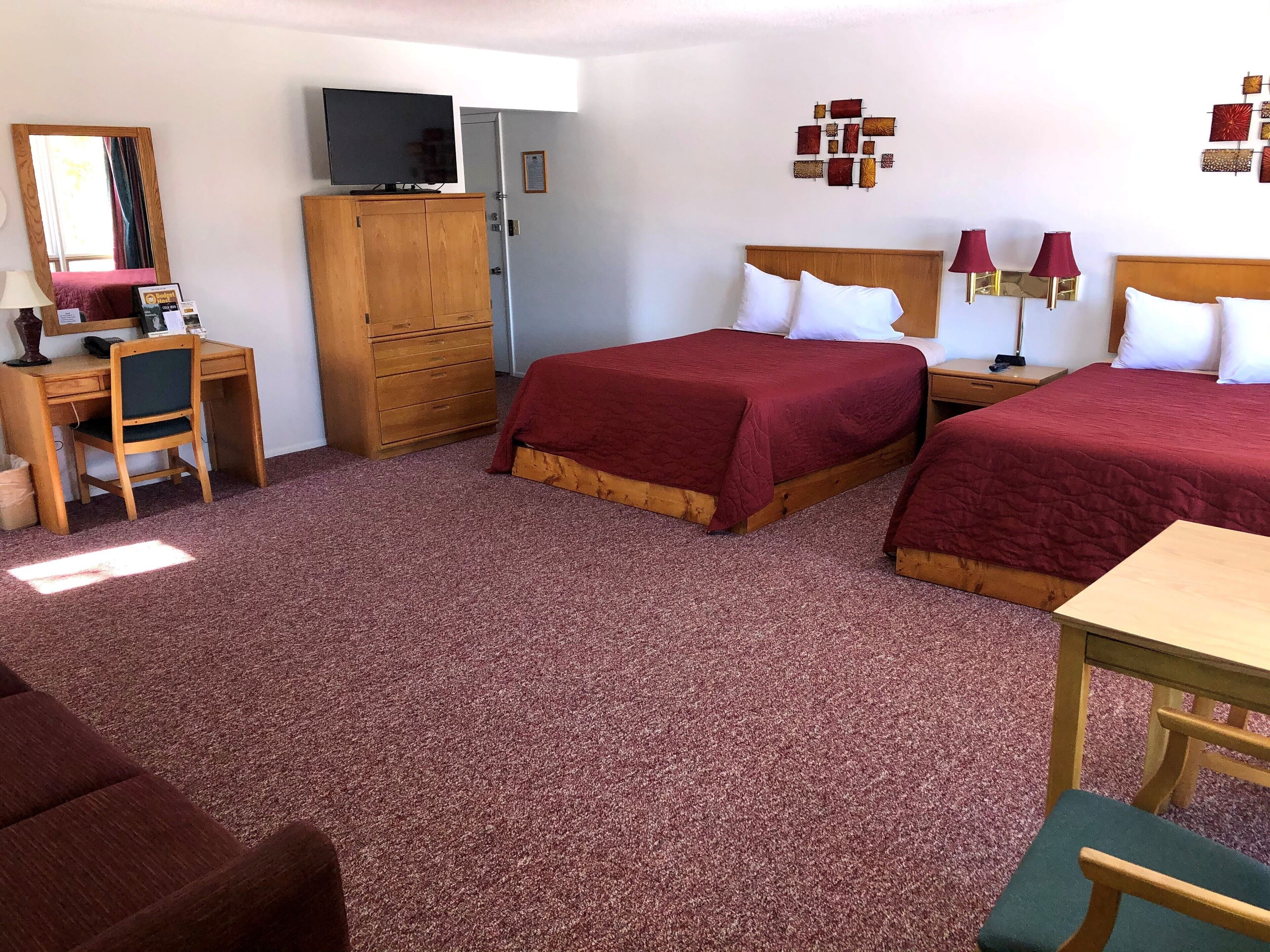 Quarto de hotel com duas camas, uma escrivaninha, uma cadeira, uma televisão e um guarda-roupa.