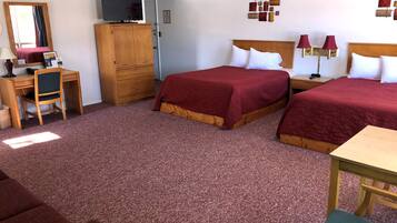 Quarto de hotel com duas camas, uma escrivaninha, uma cadeira, uma televisão e um guarda-roupa.