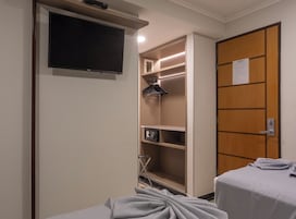 Quarto de hotel com uma cama, televisão, guarda-roupa e um armário com casaco e cofre.