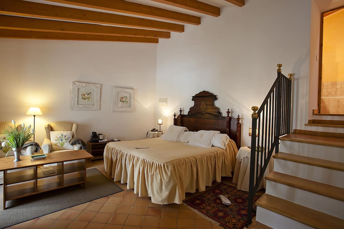 Um quarto com cama, mesa de cabeceira, abajur, cadeira e escada.