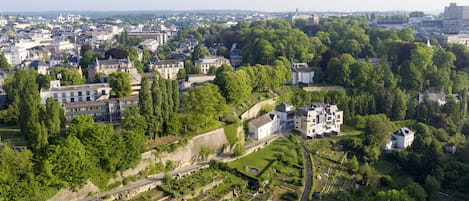 Vista aérea de uma cidade histórica com mistura de edifícios residenciais e comerciais, cercada por vegetação exuberante e jardins bem cuidados.