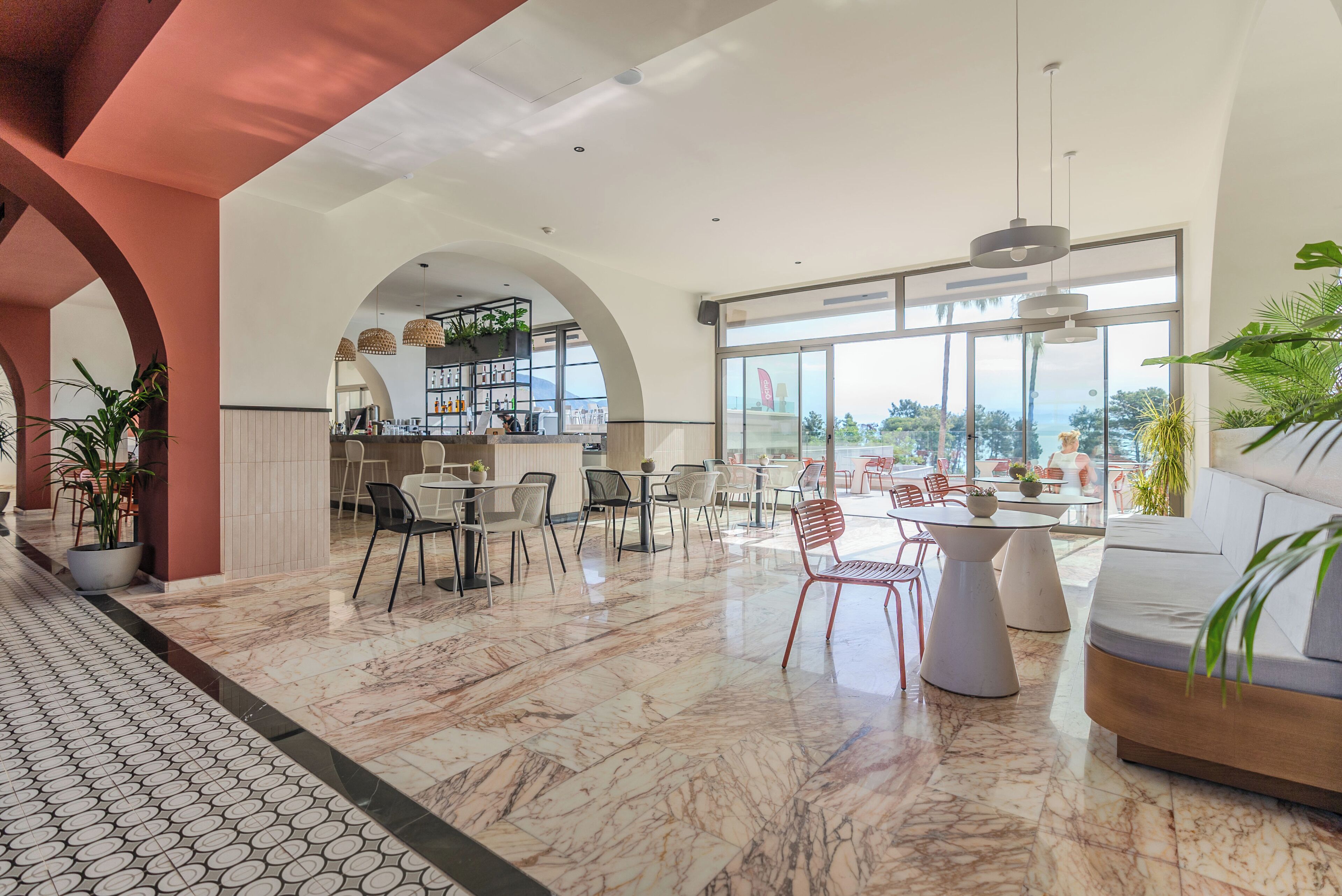 Um espaço interno amplo com piso de mármore, móveis modernos e grandes janelas com vista para o exterior.