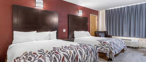 Quarto de hotel com duas camas, cabeceira de madeira, janela com cortinas e luminária fixada na parede.