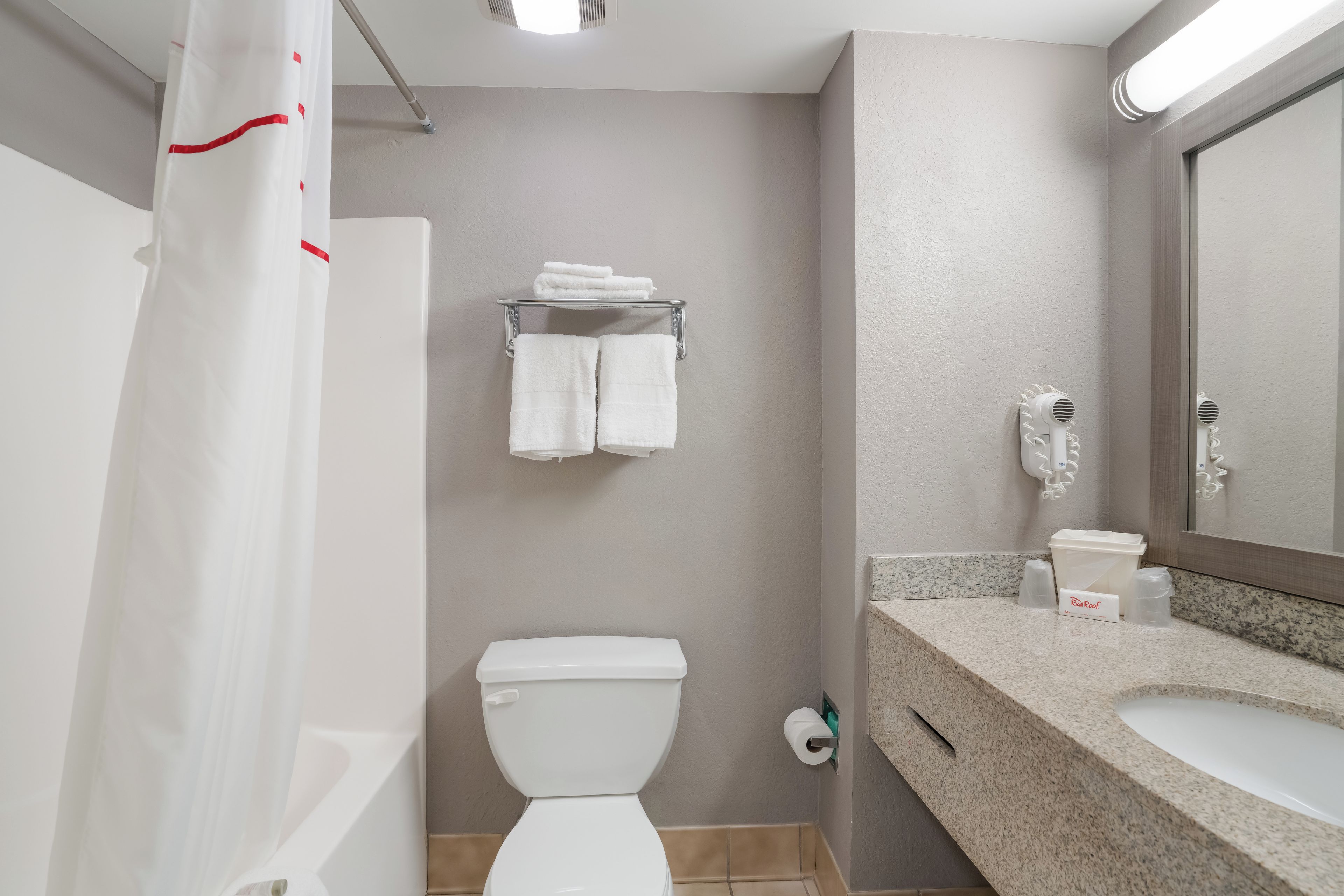 Casa de banho com sanita, porta-toalhas, cortina de chuveiro, secador de cabelo e lavatório com bancada.