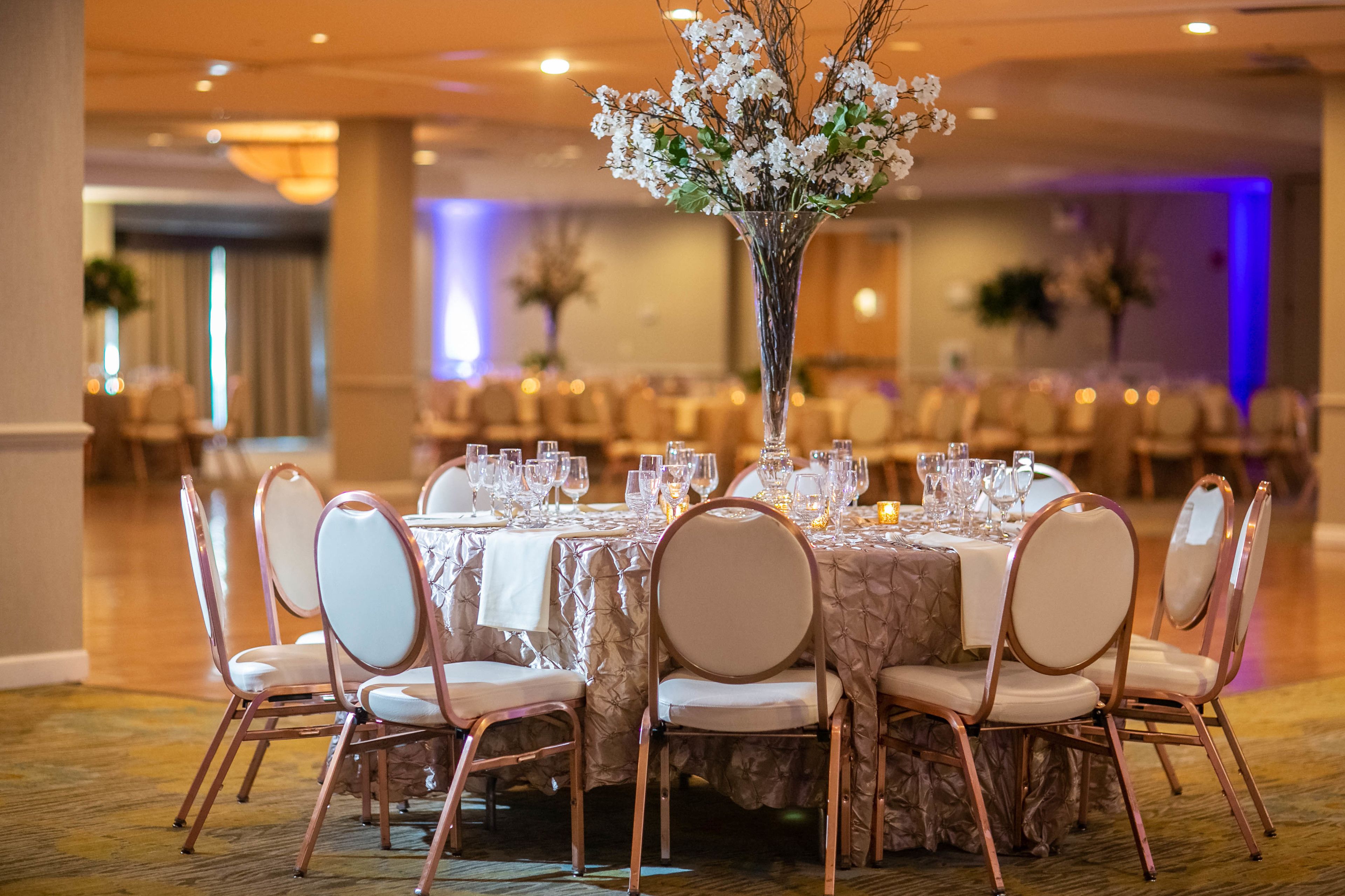Uma sala de banquetes com mesas redondas preparadas para refeições, cada uma com toalha branca e cadeiras combinando.