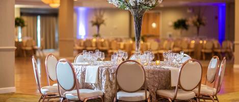 Uma sala de banquetes com mesas redondas preparadas para refeições, cada uma com toalha branca e cadeiras combinando.